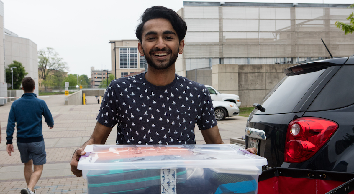 A student moving out of the residence halls carrying a large tote